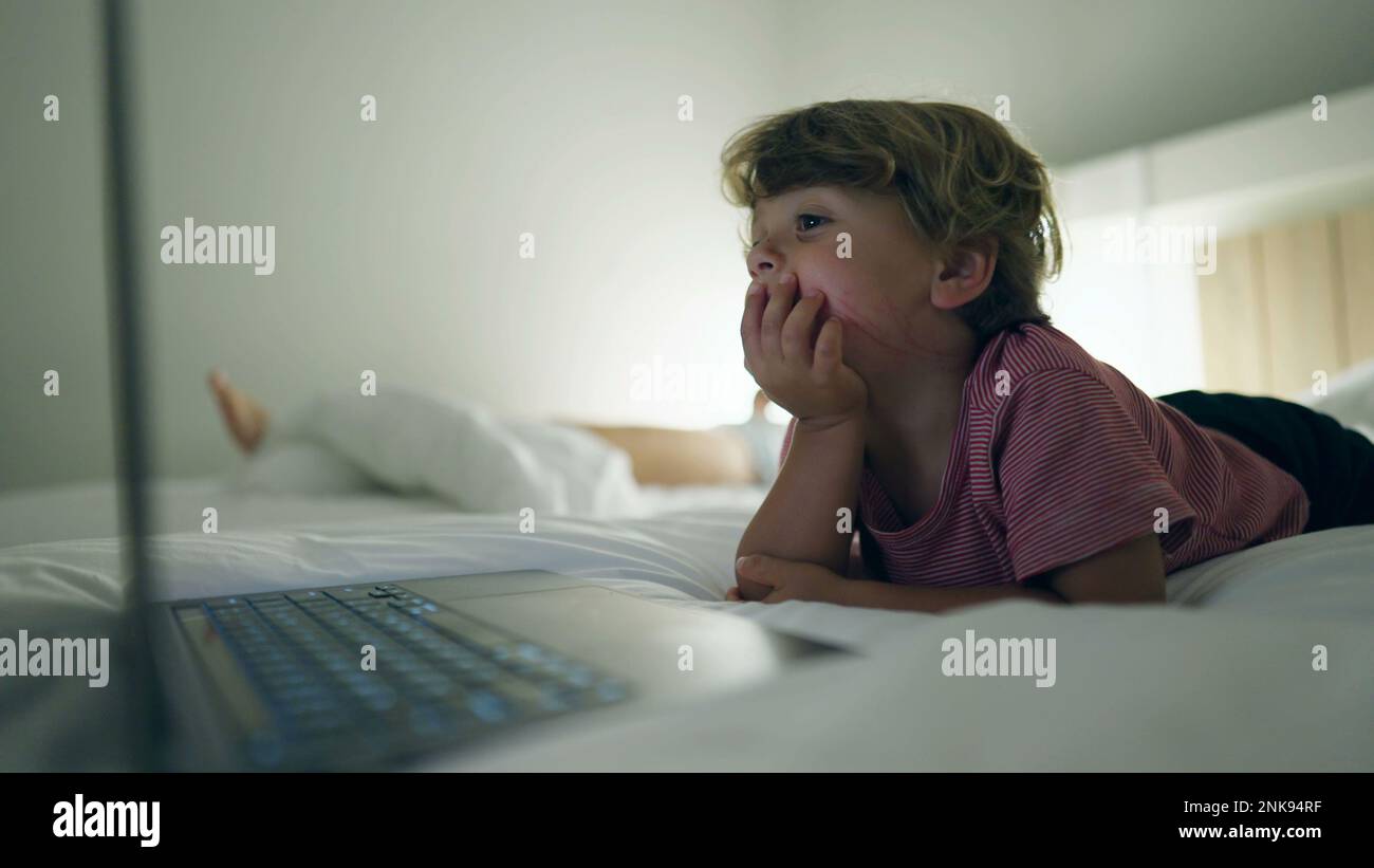 Young boy starring at media entertainment on laptop screen laying in ...