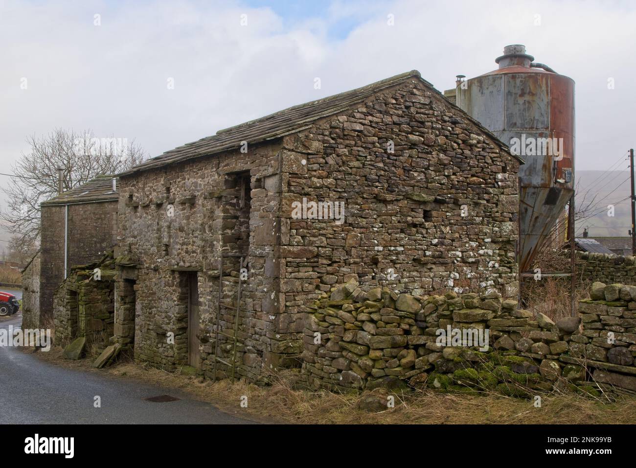 An old stone farm building stands on the edge of a country road in ...