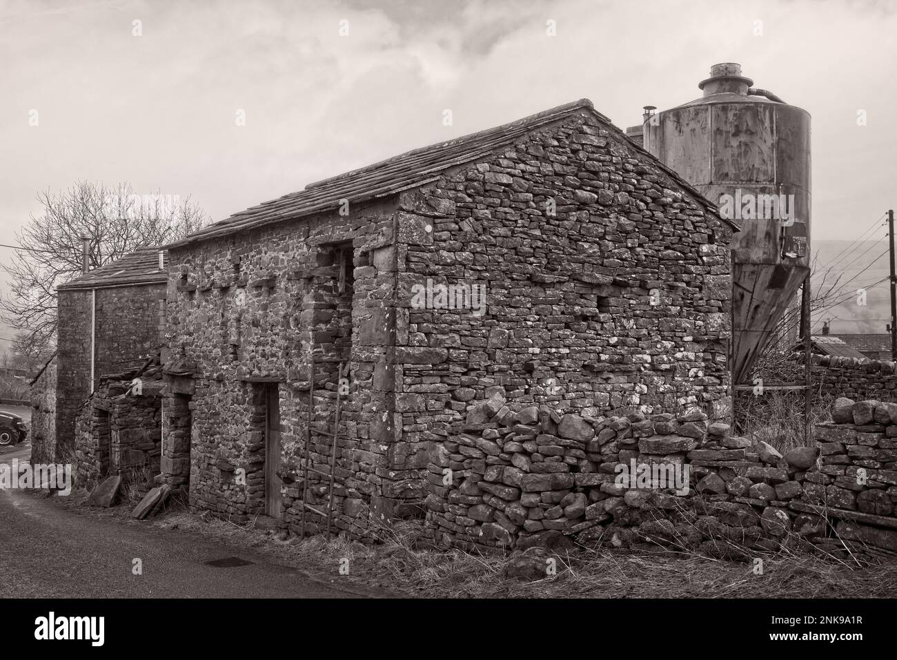 An old stone farm building stands on the edge of a country road in ...