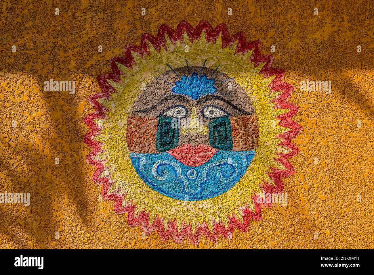 A colorful mural of a sun face painted on the wall of a buidling in ...