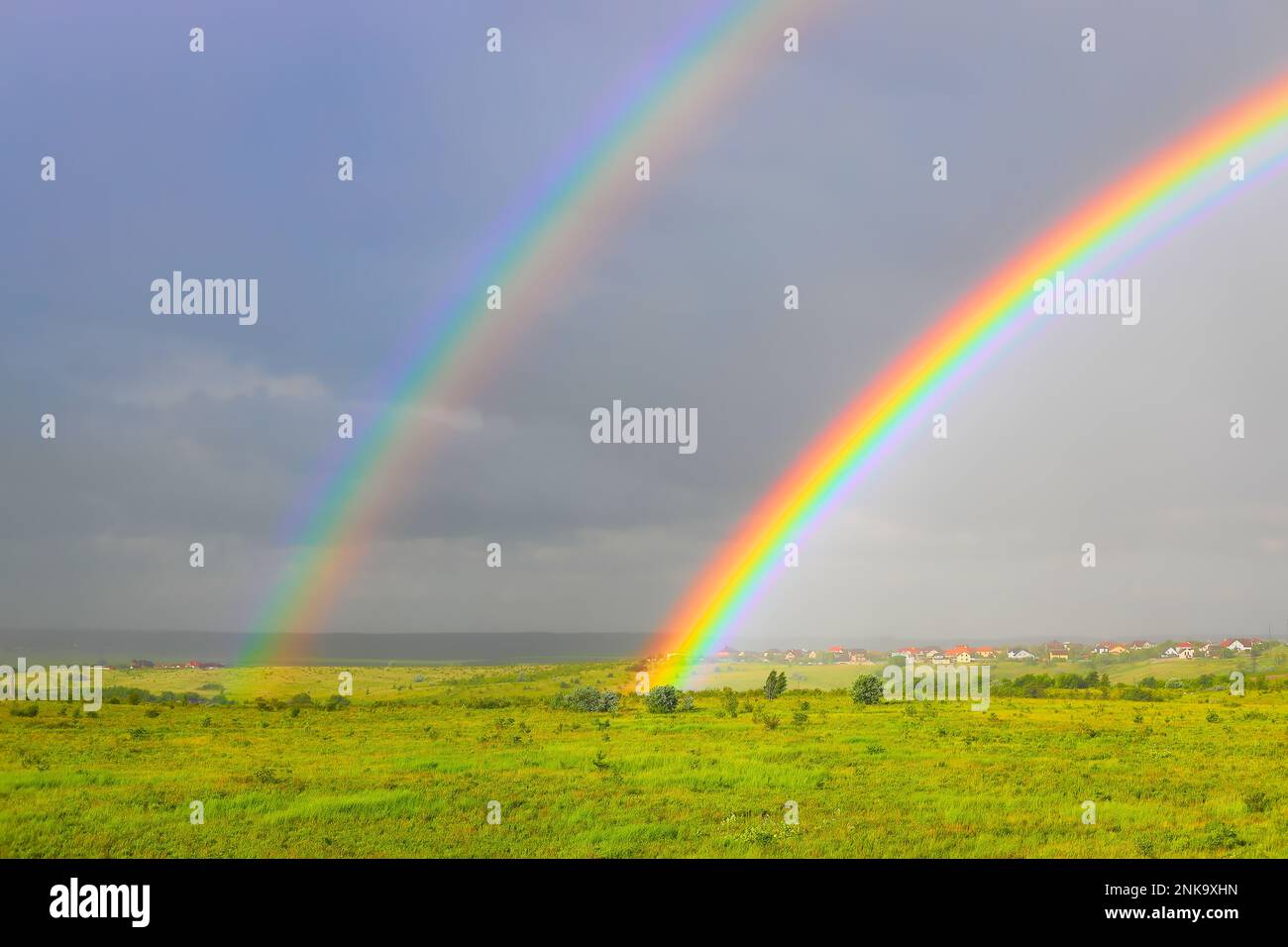 Bright colors of double rainbow rising from a meadow with dark rain ...