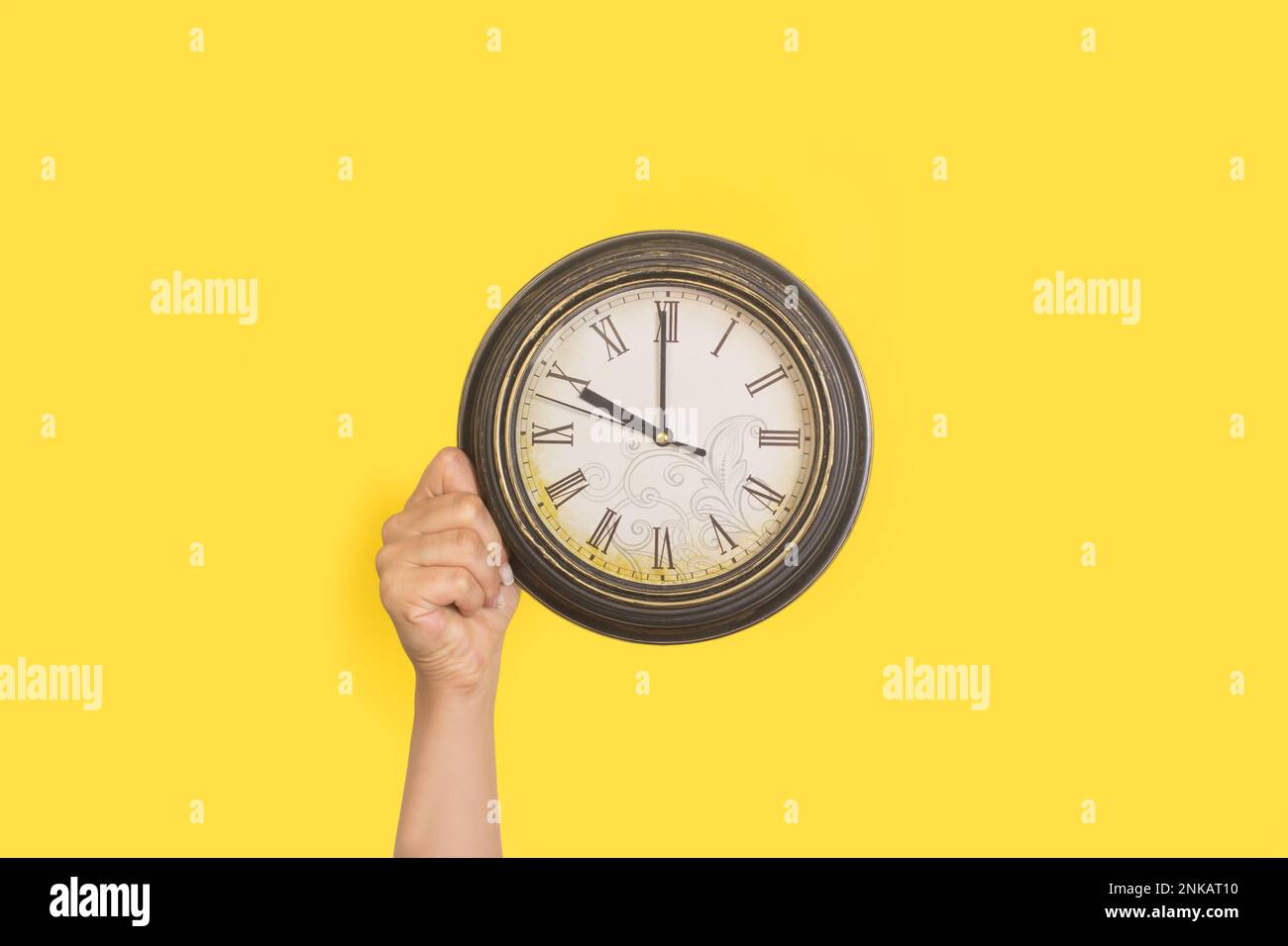 Woman hand holding a wall clock on a yellow background with copy space ...