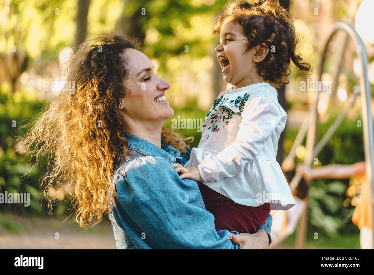 A mother holding her two-year-old daughter, both laughing and enjoying ...