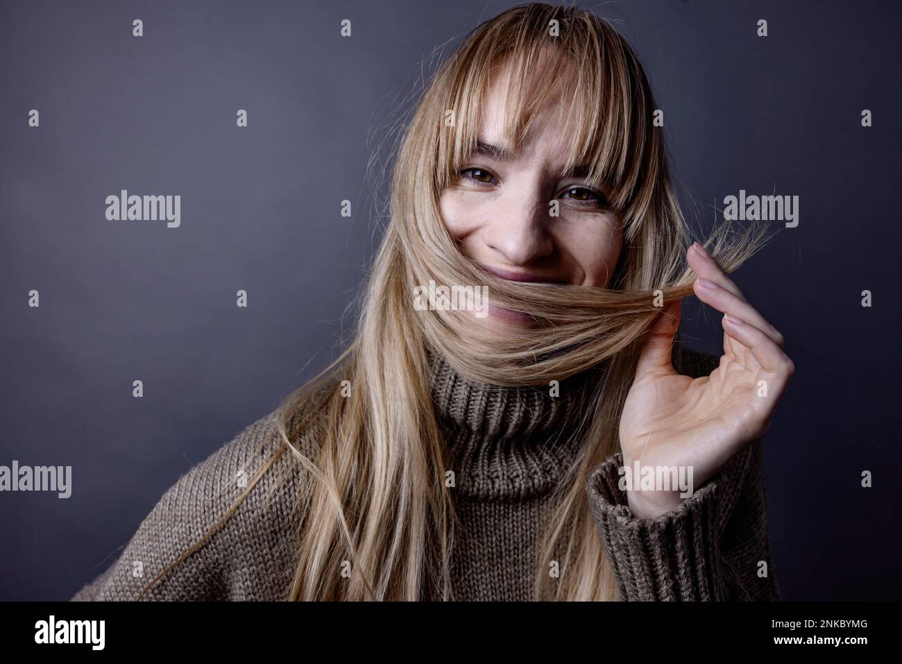 Young woman with long blond hair smiling and holding a strand of hair ...