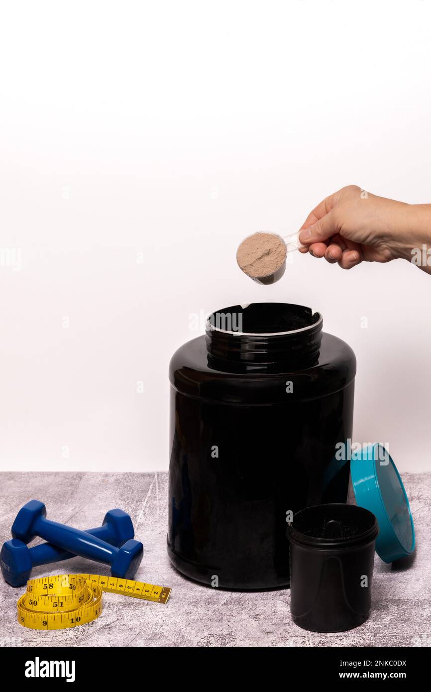 Woman pouring a scoop of protein powder in an insulated shaker on a ...