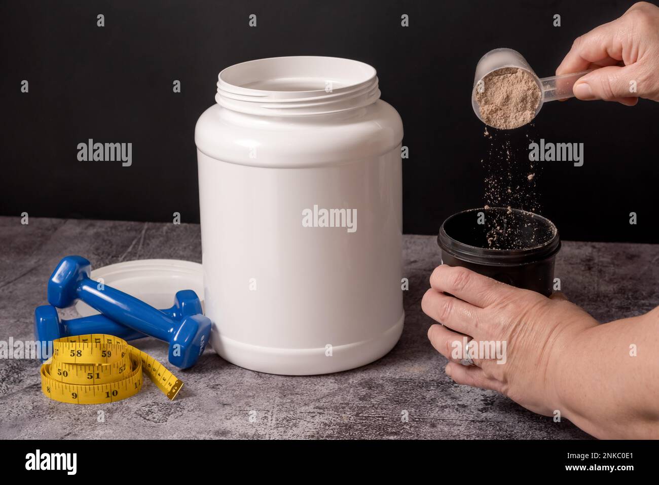 Woman pouring a scoop of protein powder in an insulated shaker on a ...