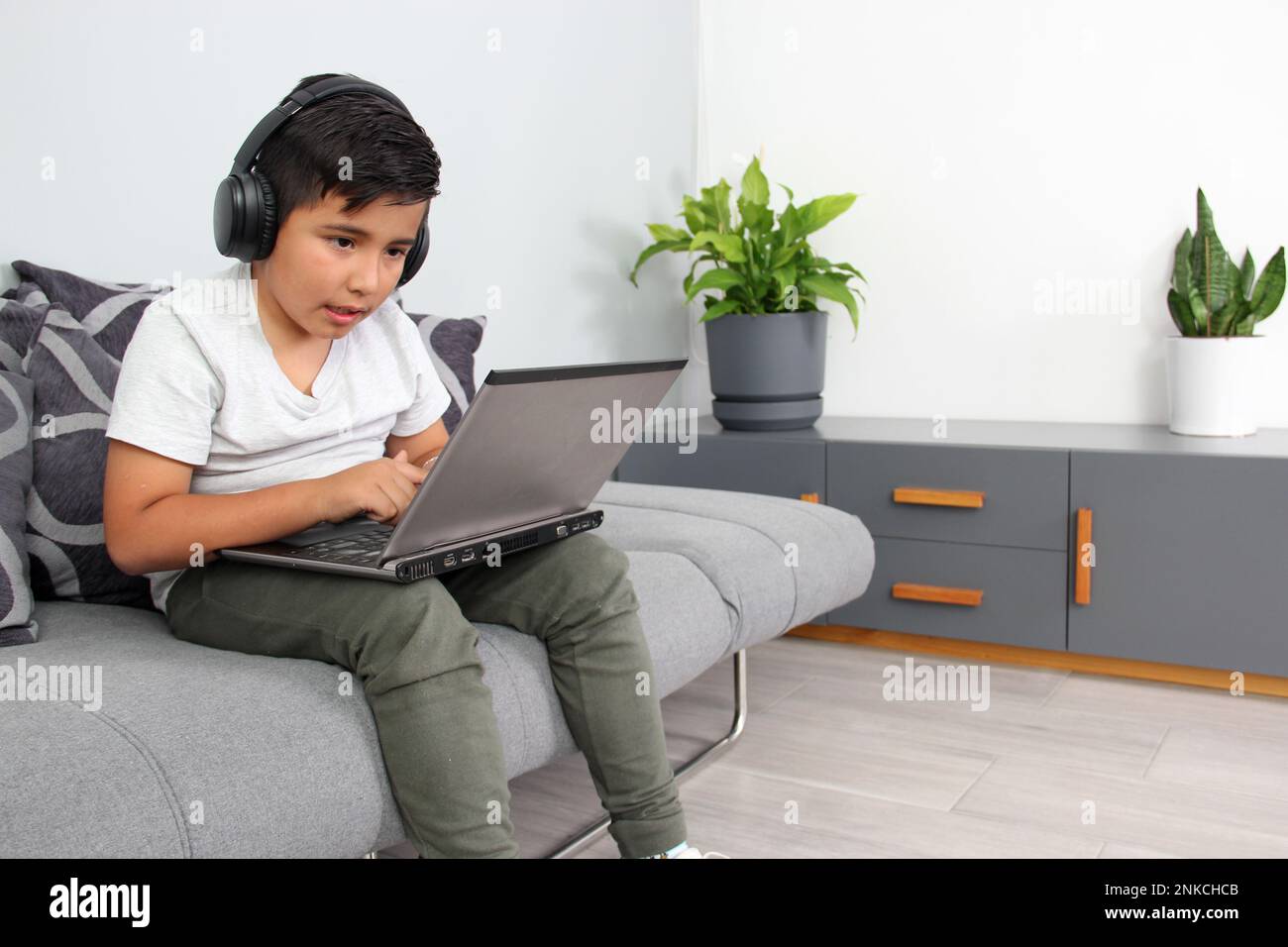 9-year-old Hispanic boy plays video games on his laptop with headphones ...