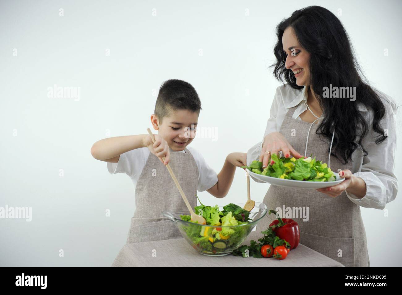 mom and son cooking fresh vegetable salad boy happy stirs food with two ...
