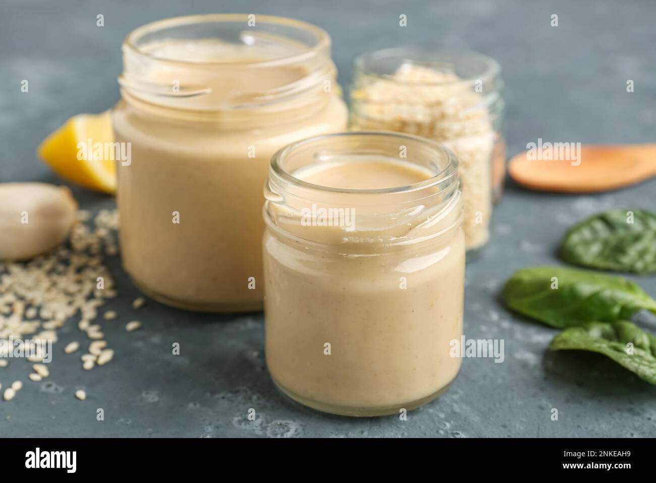 Glass jars with tasty tahini, sesame seeds and spinach on dark ...