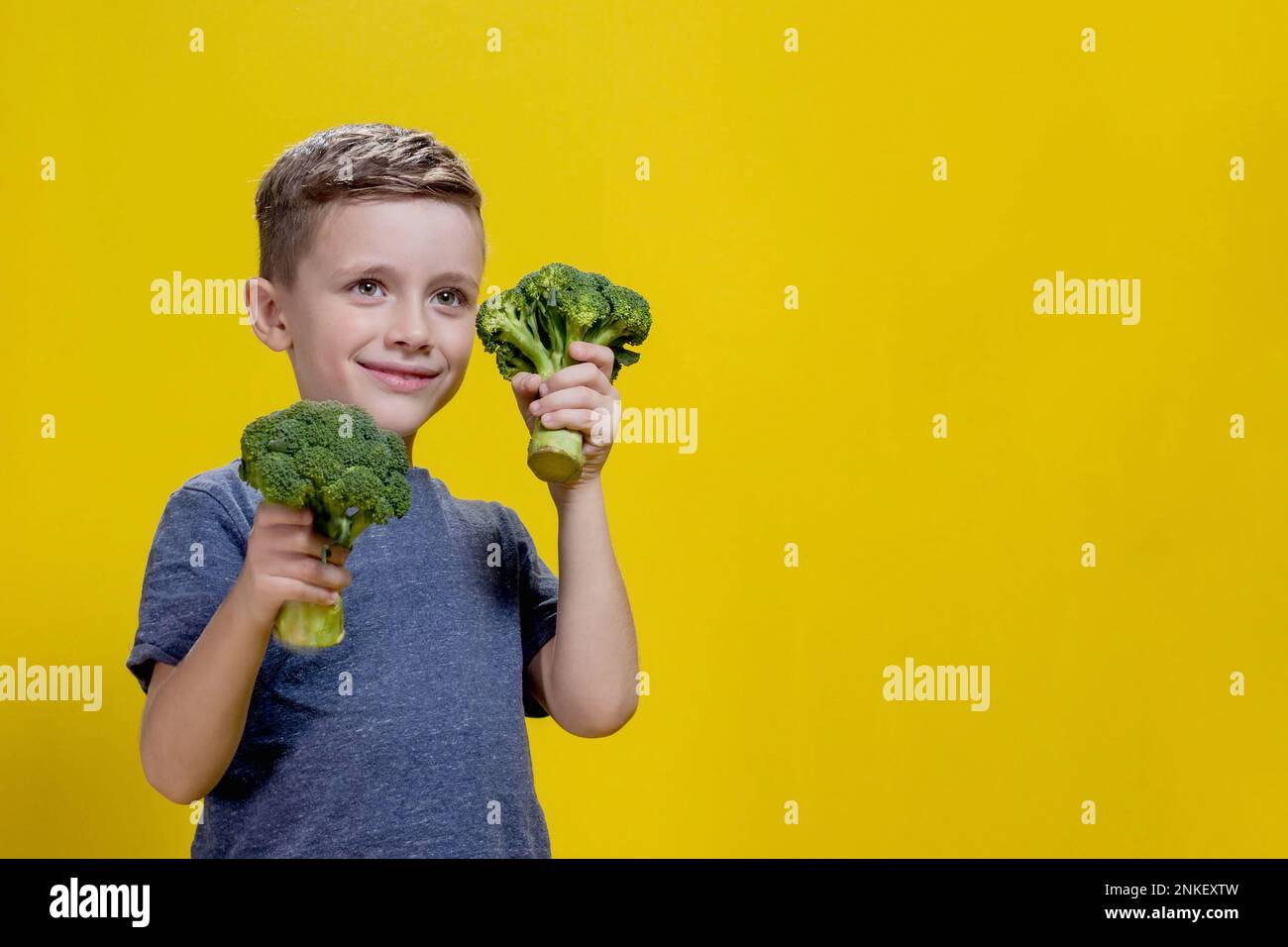 Healthy food, green vegetables broccoli in the hands of a cheerful boy ...