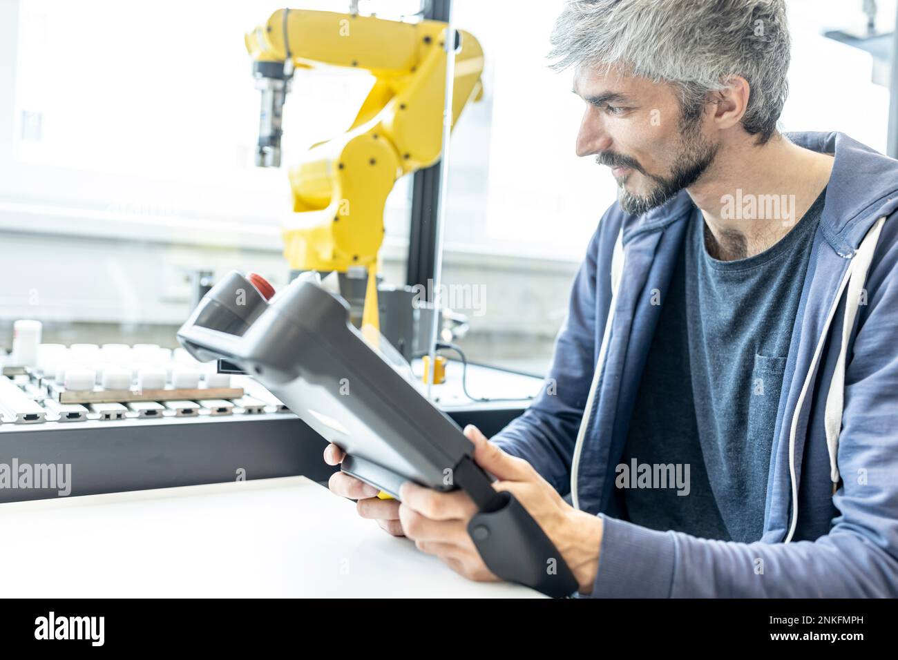 Skilled worker in robotic factory controlling robot arm with digital ...