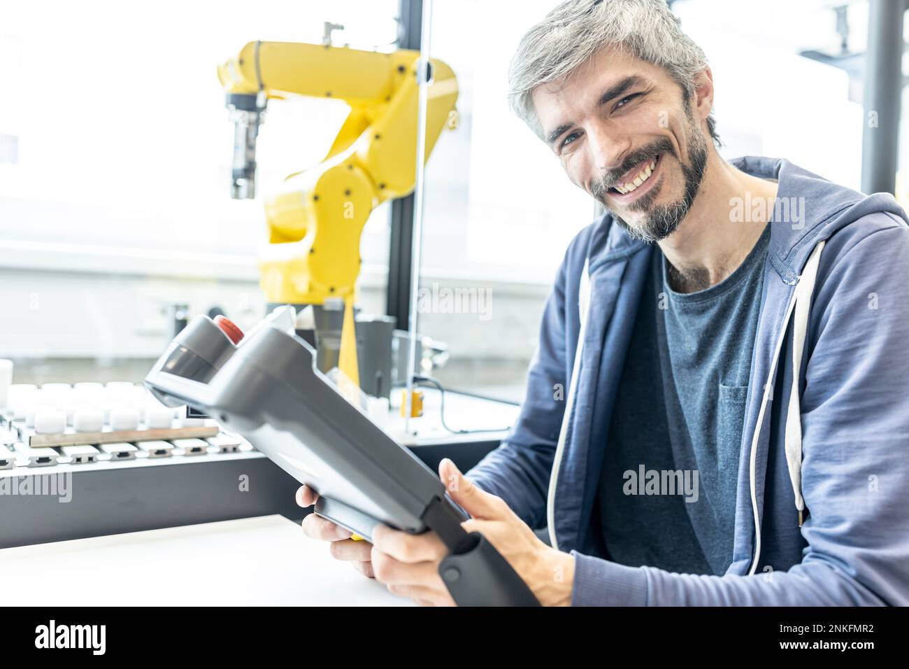 Skilled worker in robotic factory controlling robot arm with digital ...