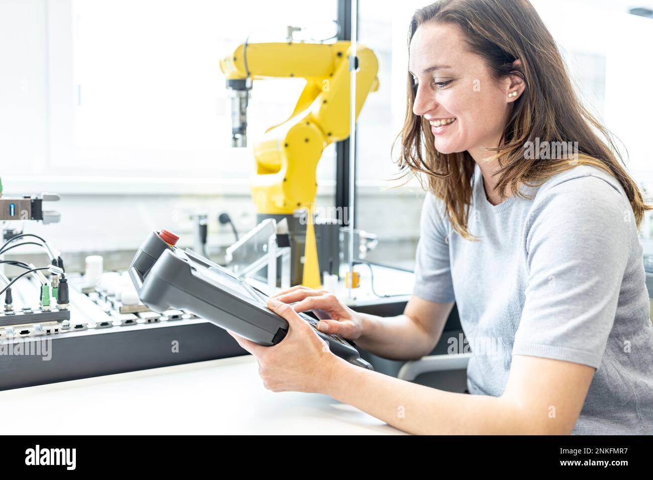 Female skilled worker in robotic factory controlling robot arm with ...