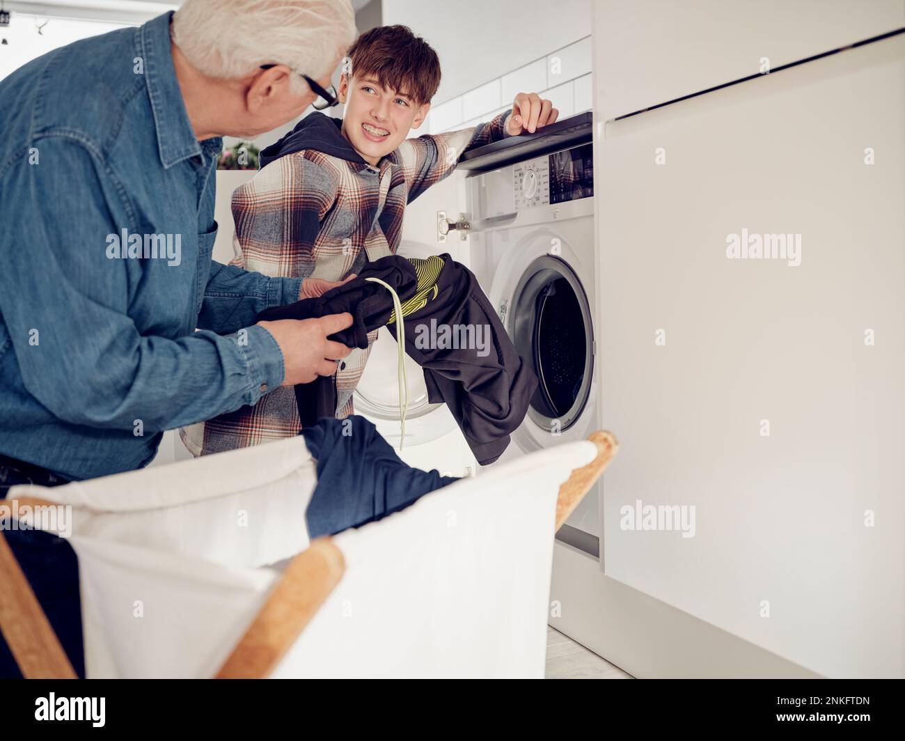 Grandson and grandfather putting laundry into washing machine at home ...