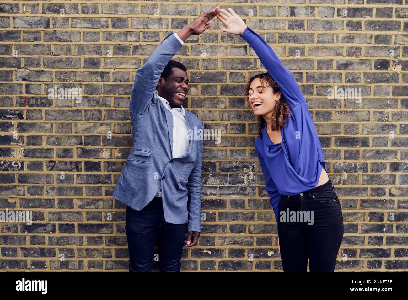 Businesswoman and colleague having fun standing in front of brick wall ...