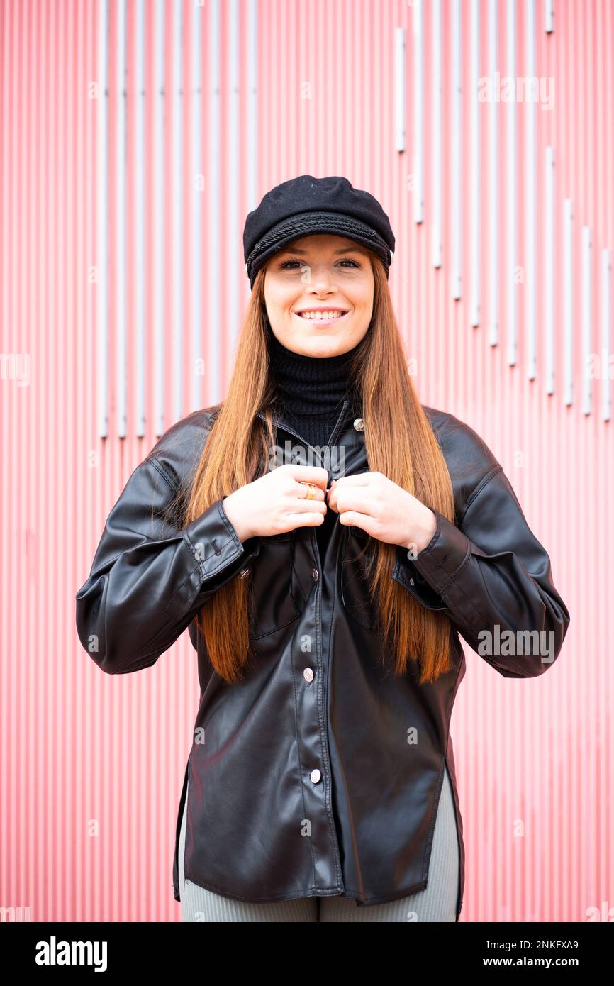 Happy redhead woman wearing cap and jacket in front of pink wall Stock ...