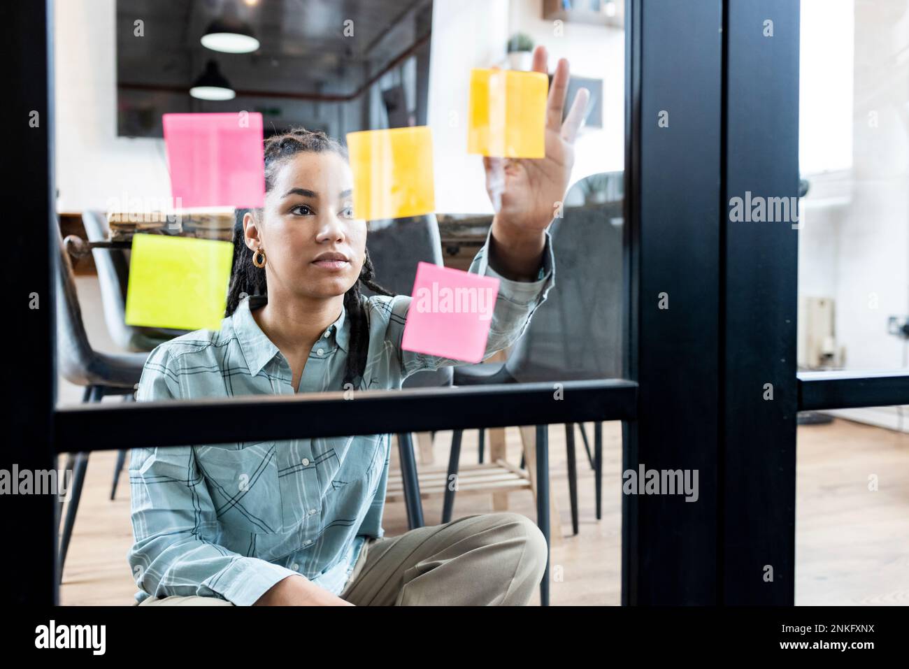 Businesswoman sticking adhesive notes on glass in office Stock Photo ...