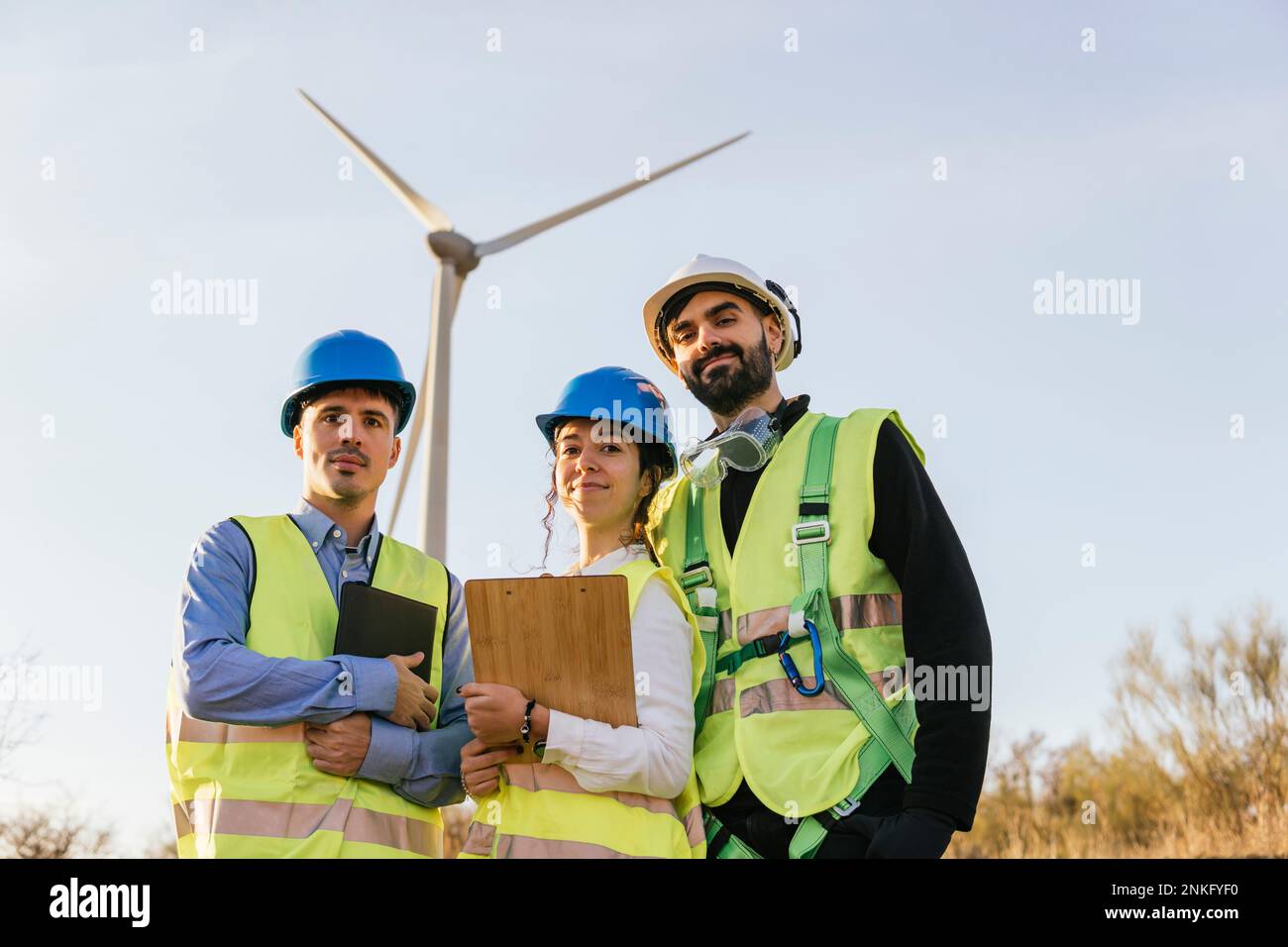 Smiling engineers and technician standing in front of wind turbine ...