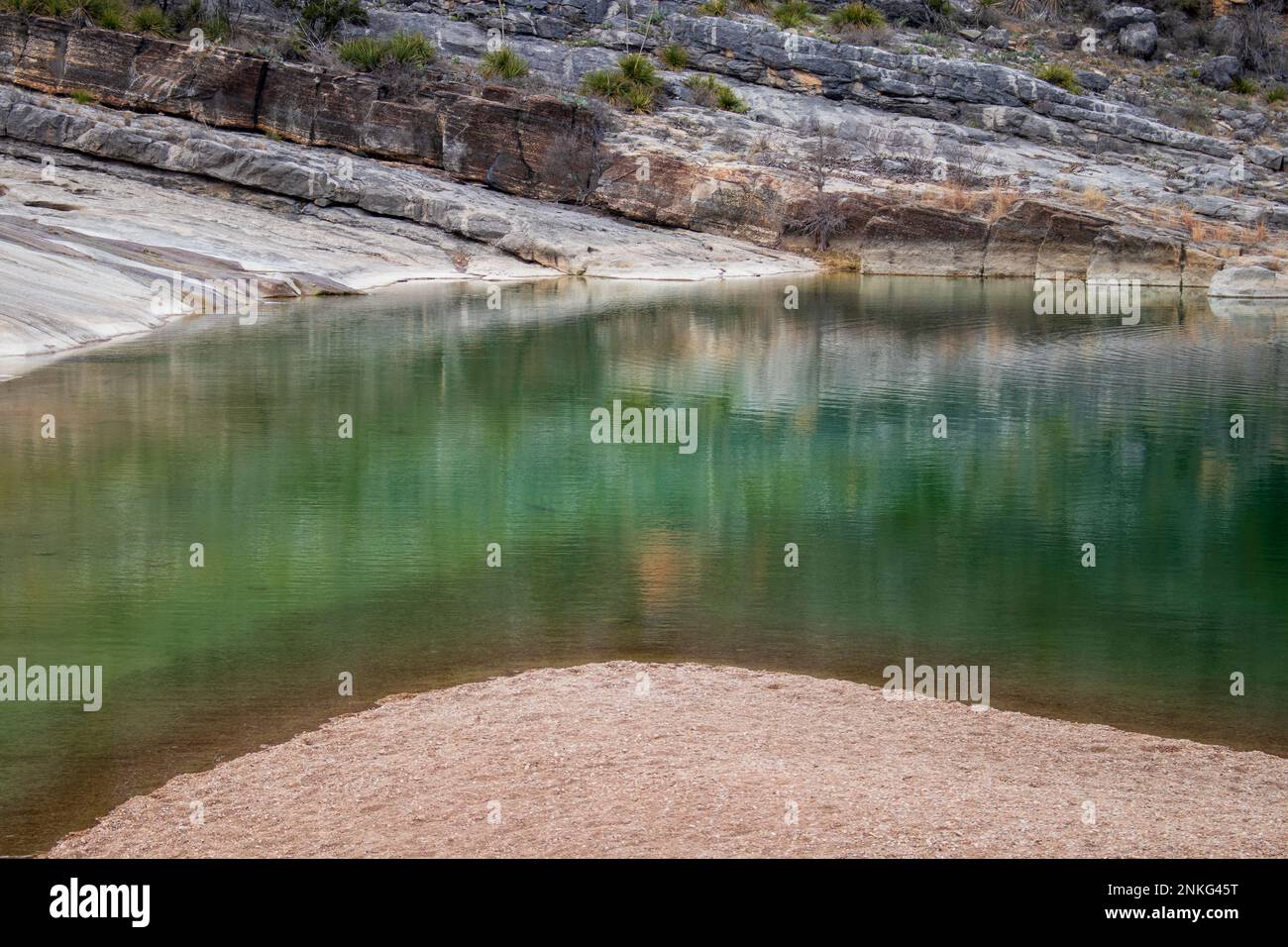 Geological granite stone and limestone wall mirrored in a green pond ...