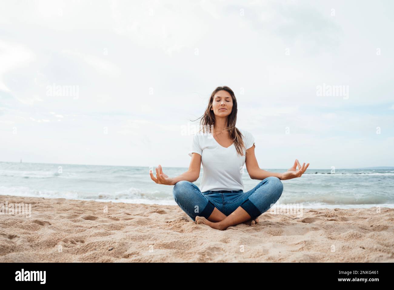 Woman practicing lotus position sitting cross-legged on sand at beach ...