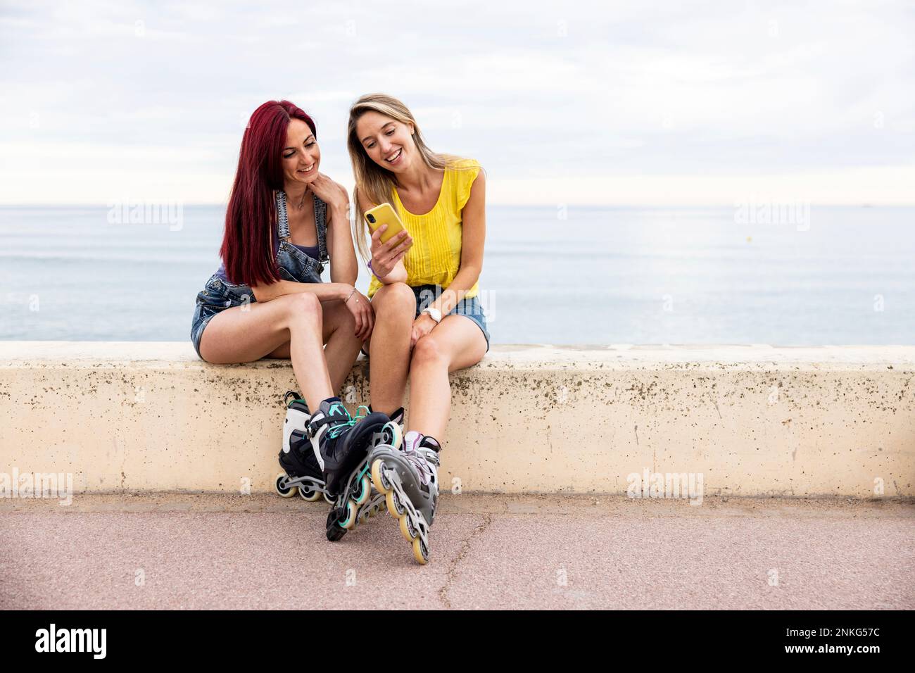 Friends wearing inline skates using smart phone at promenade in front ...