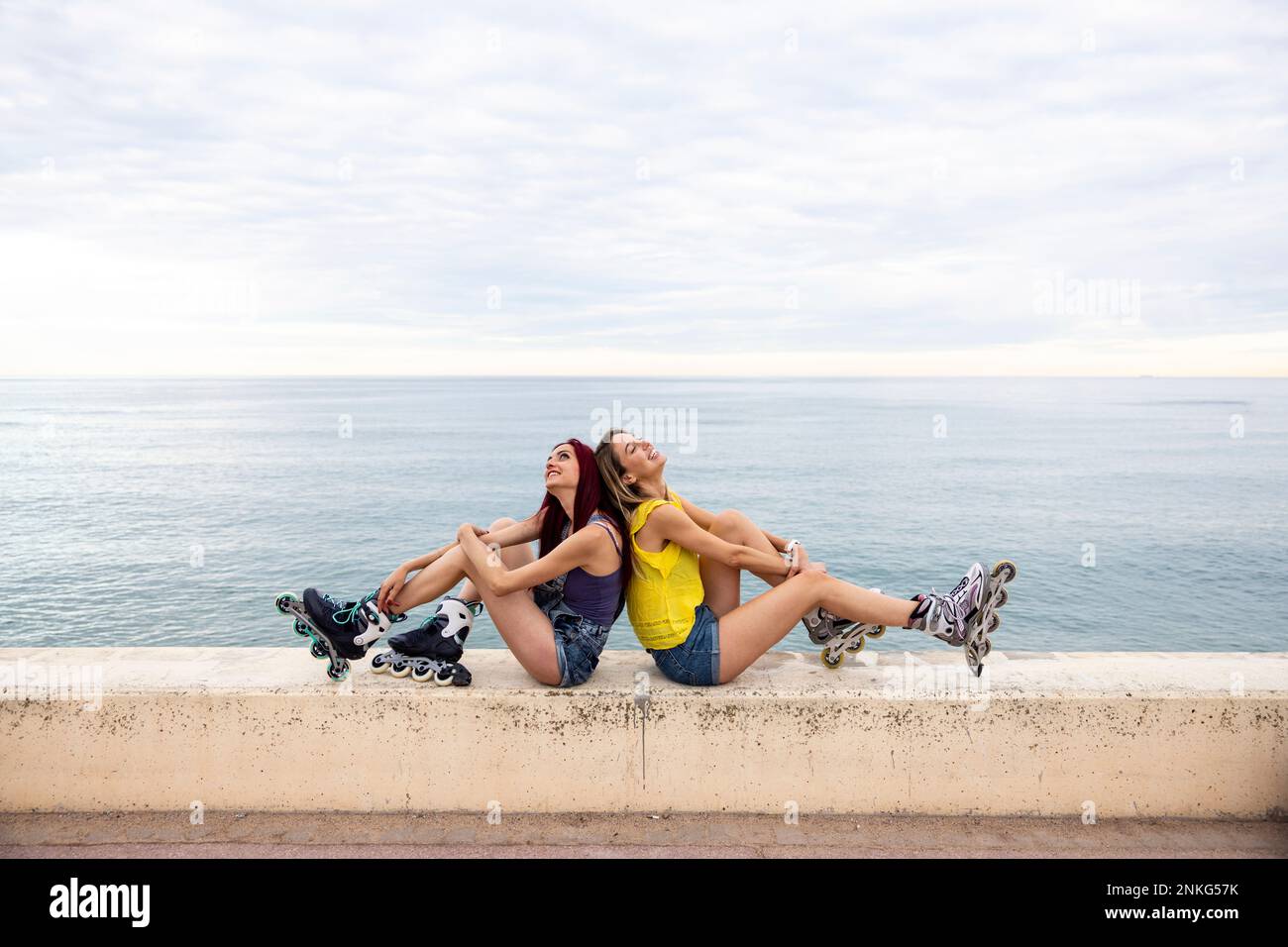 Women wearing inline skates sitting back to back at promenade by sea ...