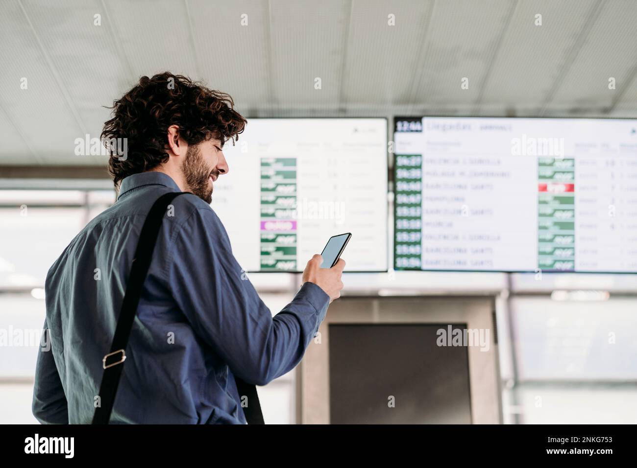 Businessman using mobile phone in front of arrival departure board ...