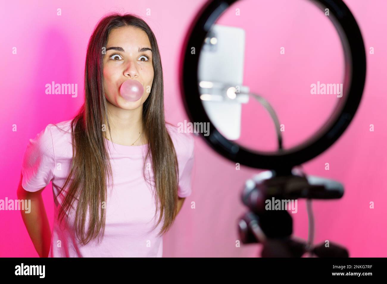 Young influencer blowing bubble gum in front of smart phone over pink ...