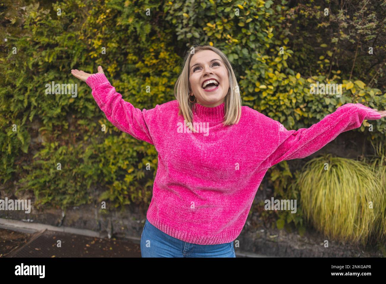 Carefree mature woman wearing pink sweater dancing in front of plants ...