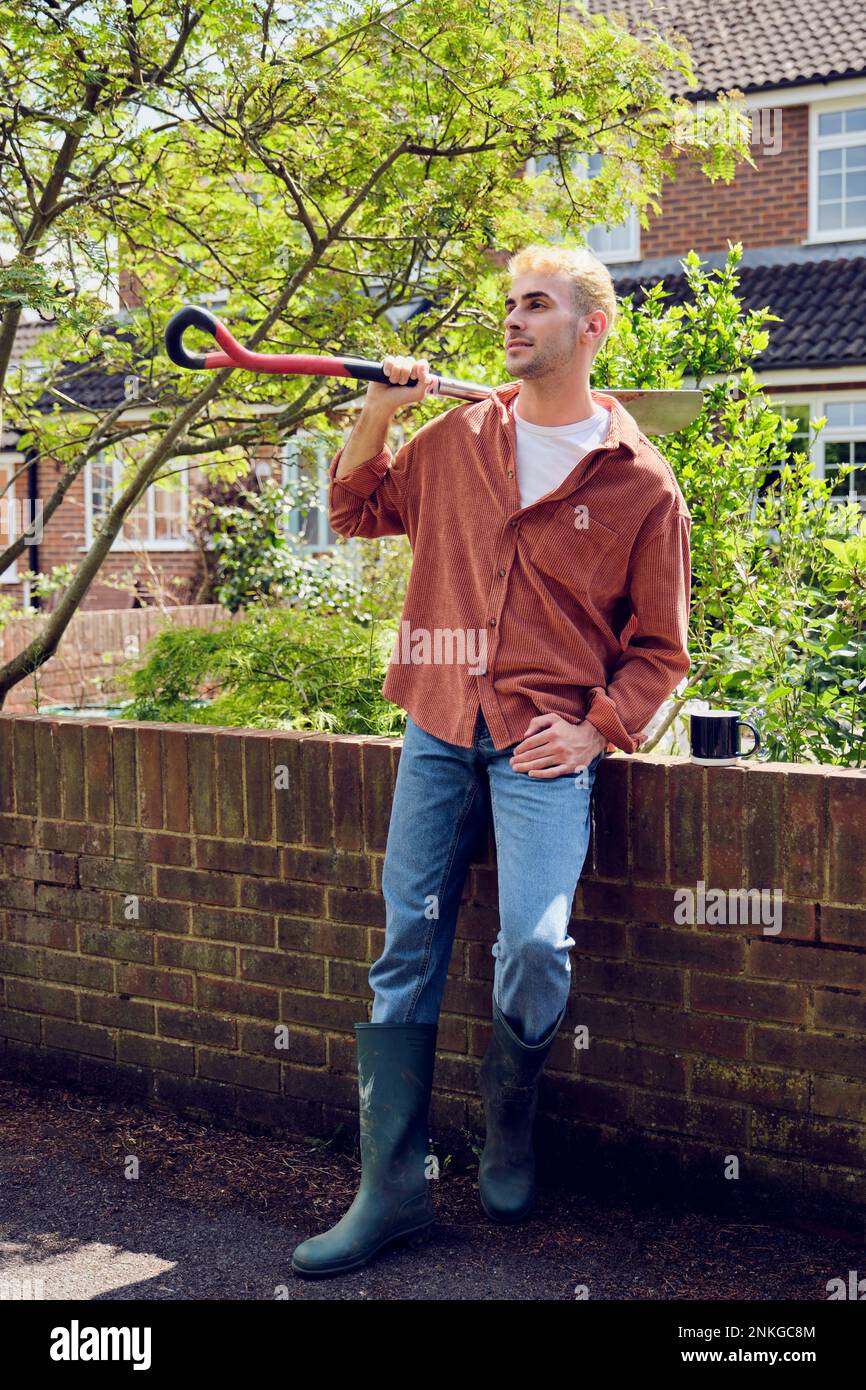 Young man holding shovel standing near fence Stock Photo - Alamy