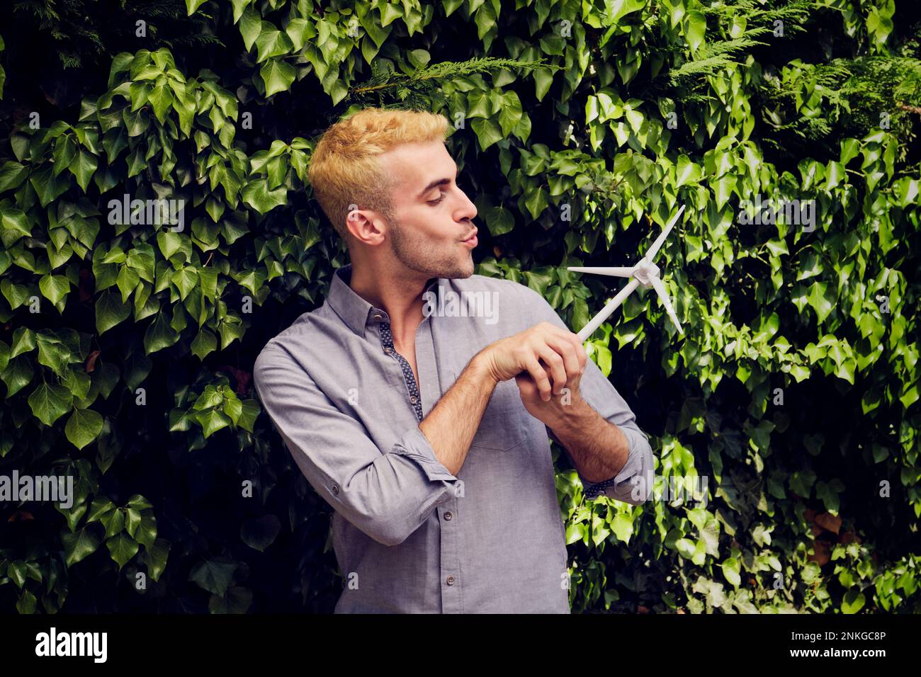 Young man blowing on wind turbine model in front of hedge Stock Photo ...