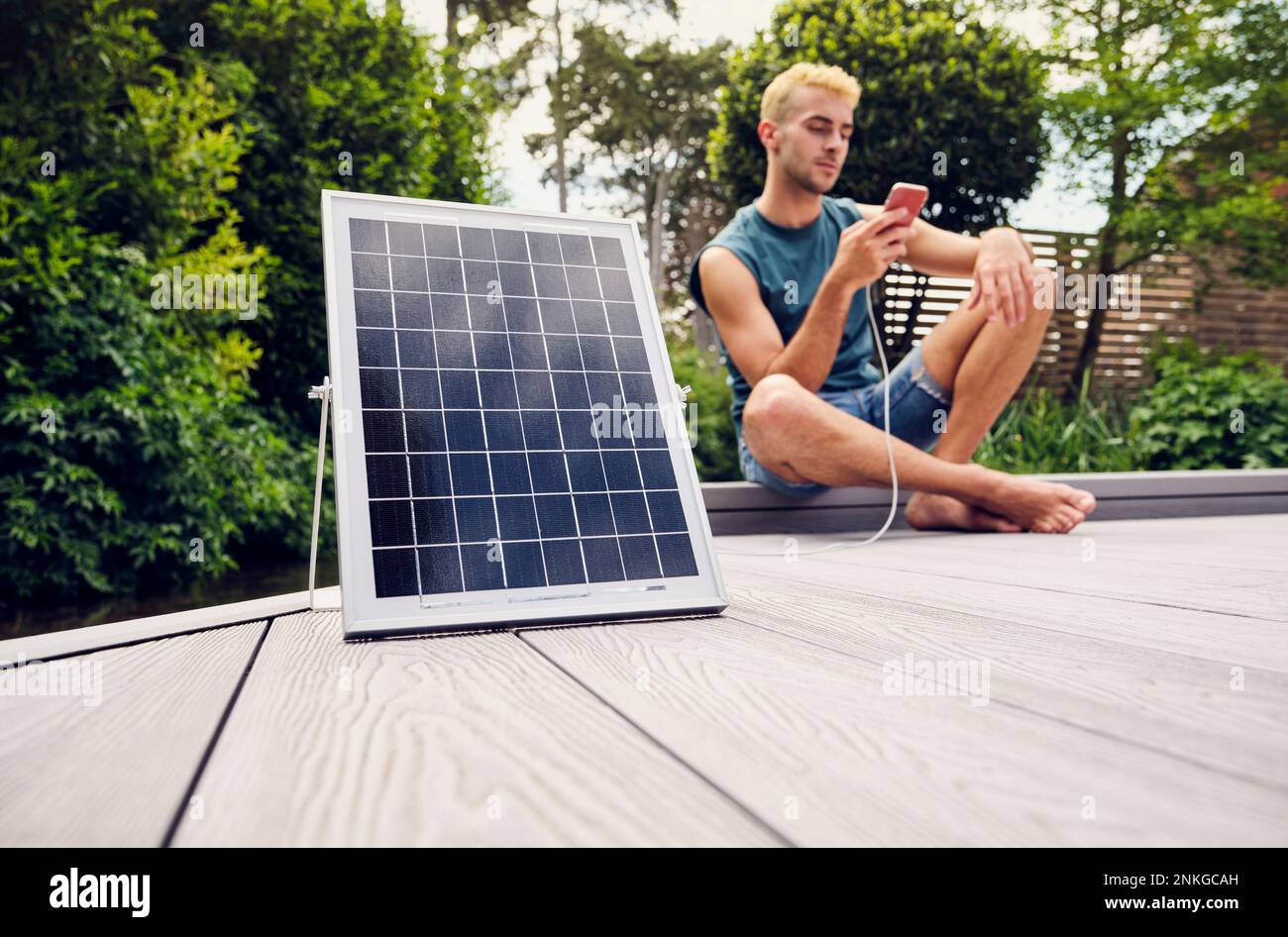 Young man sitting on patio using smart phone getting charged by solar ...