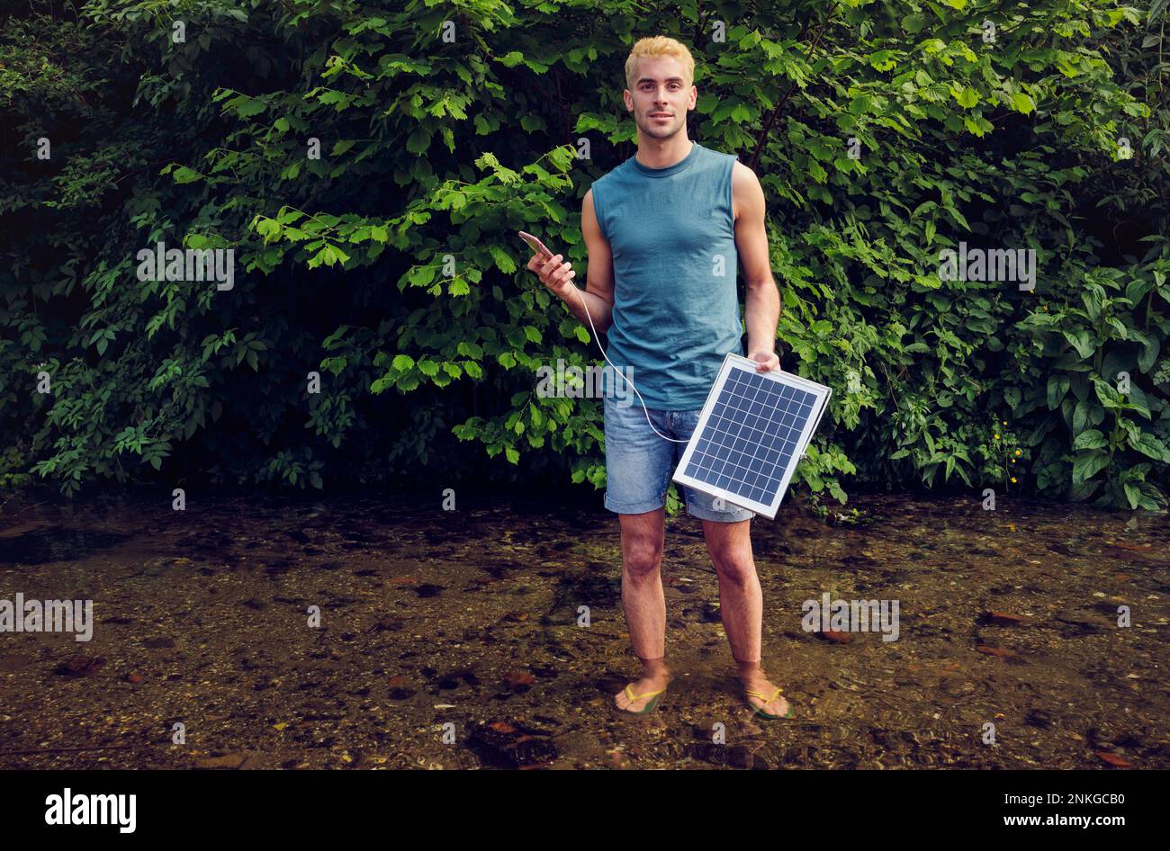 Young man standing in stream holding mobile phone getting charged by ...