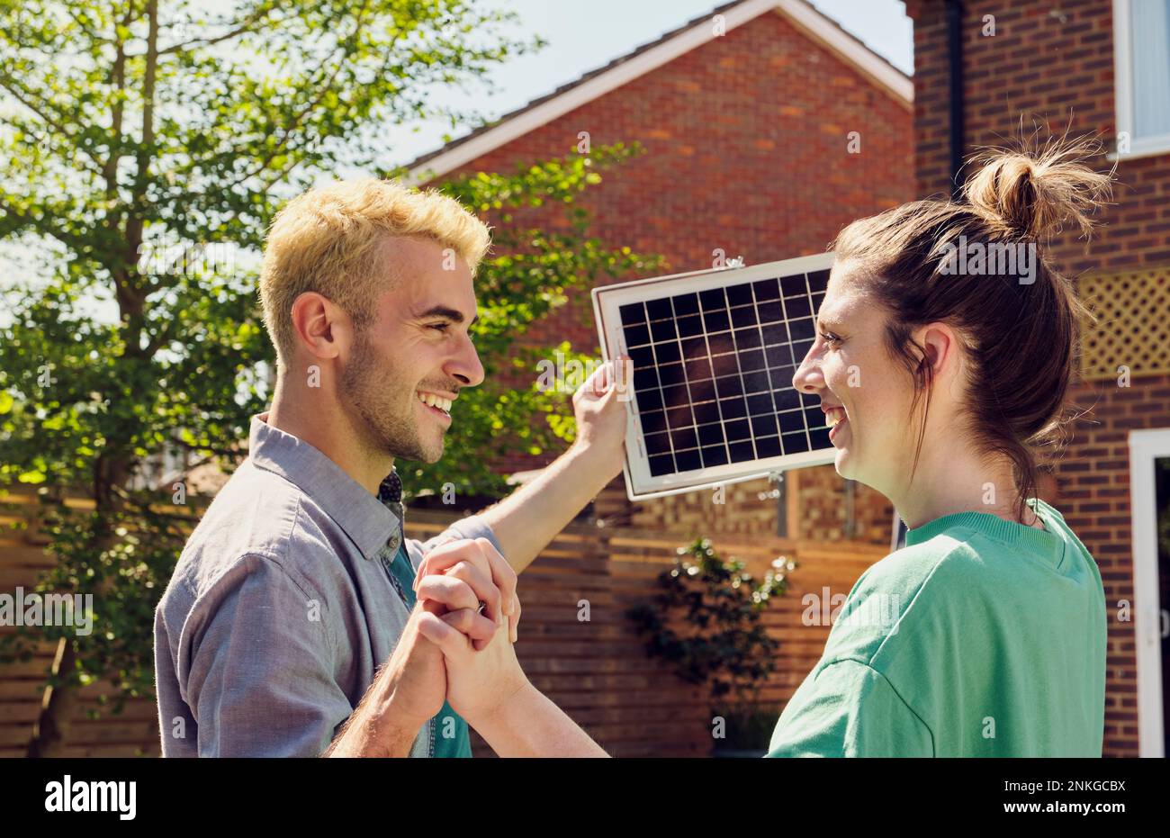 Smiling couple with hands intertwined holding solar panel in front of ...