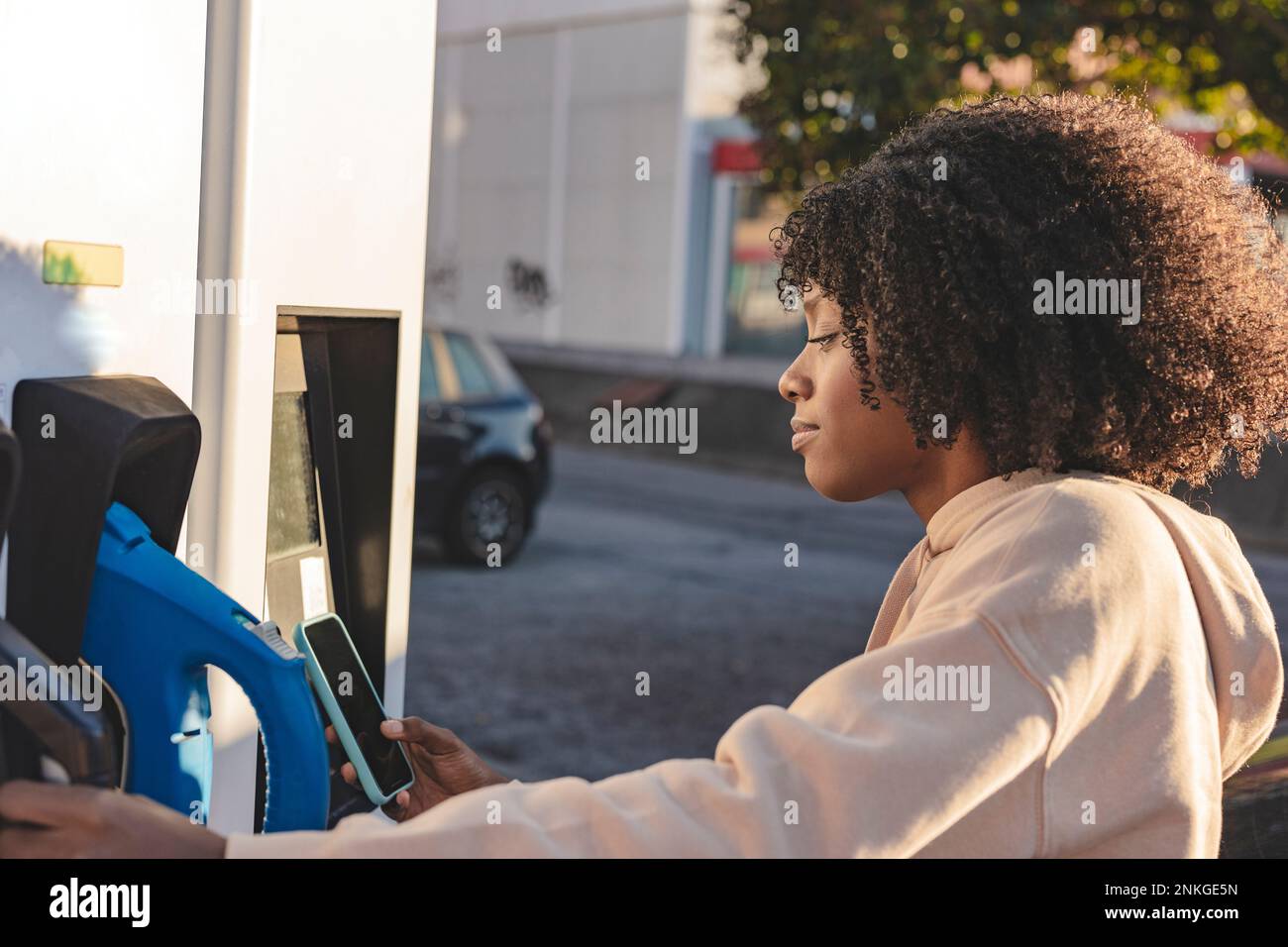 Young woman making payment through smart phone at electric vehicle ...
