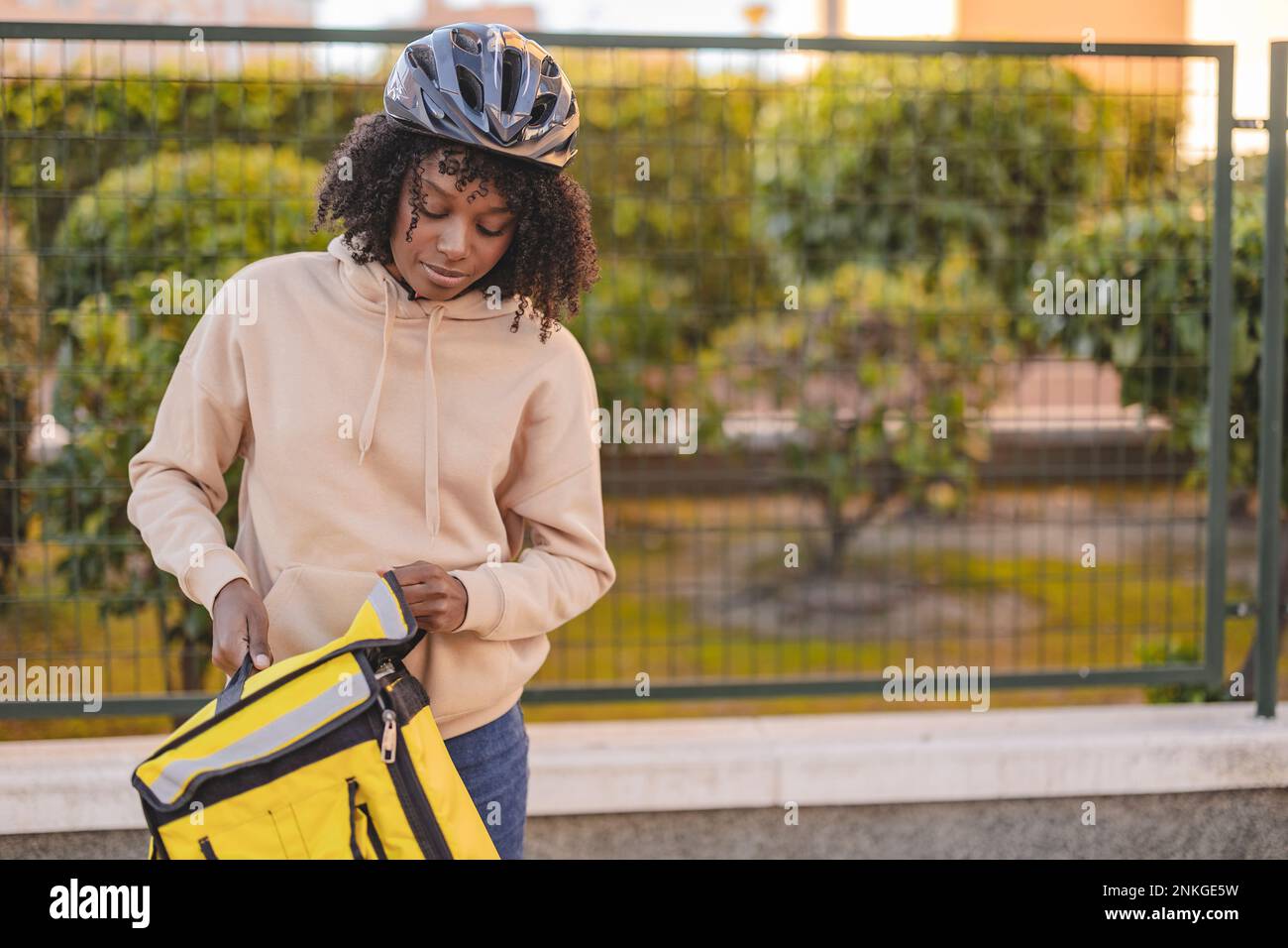 Delivery woman with yellow backpack standing in front of fence Stock ...