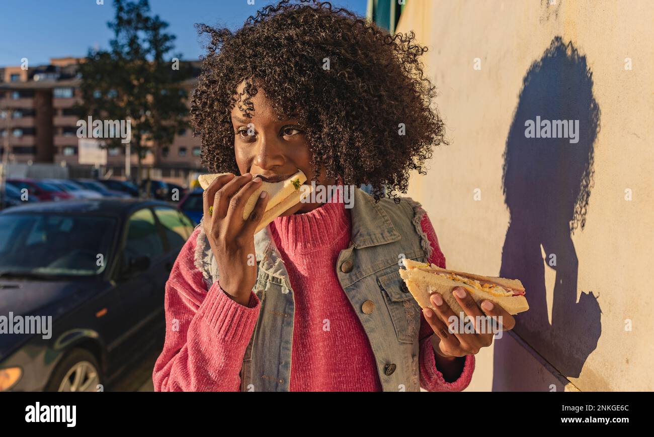 Woman eating sandwich at footpath on sunny day Stock Photo - Alamy