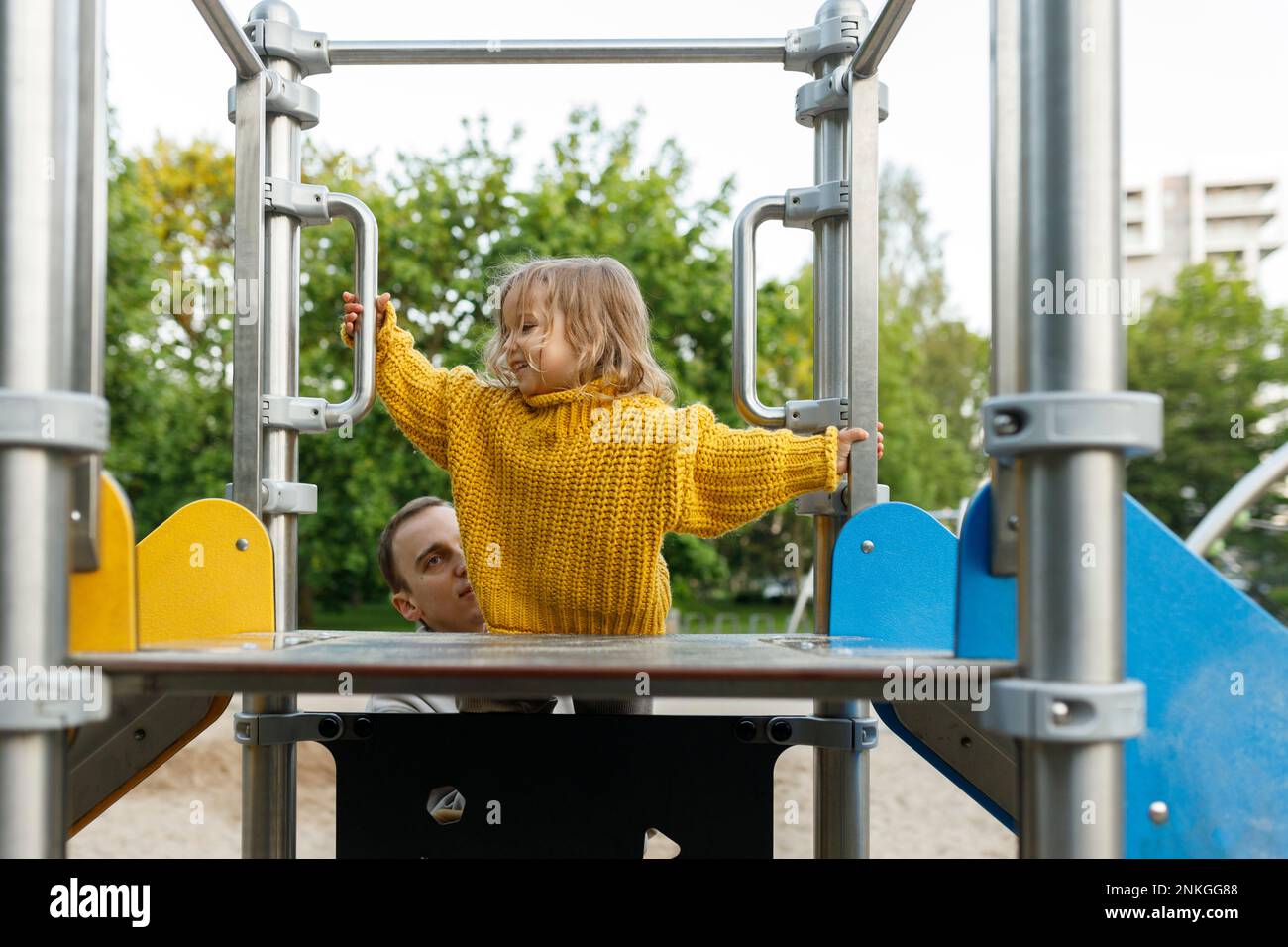 Father assisting daughter in climbing steps of slide at playground ...