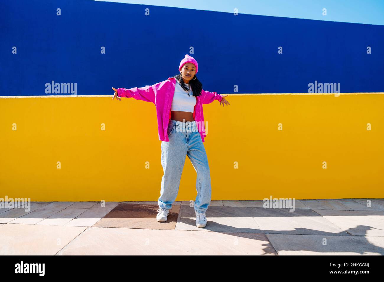 Young woman with cool attitude dancing in front of two tone color wall ...