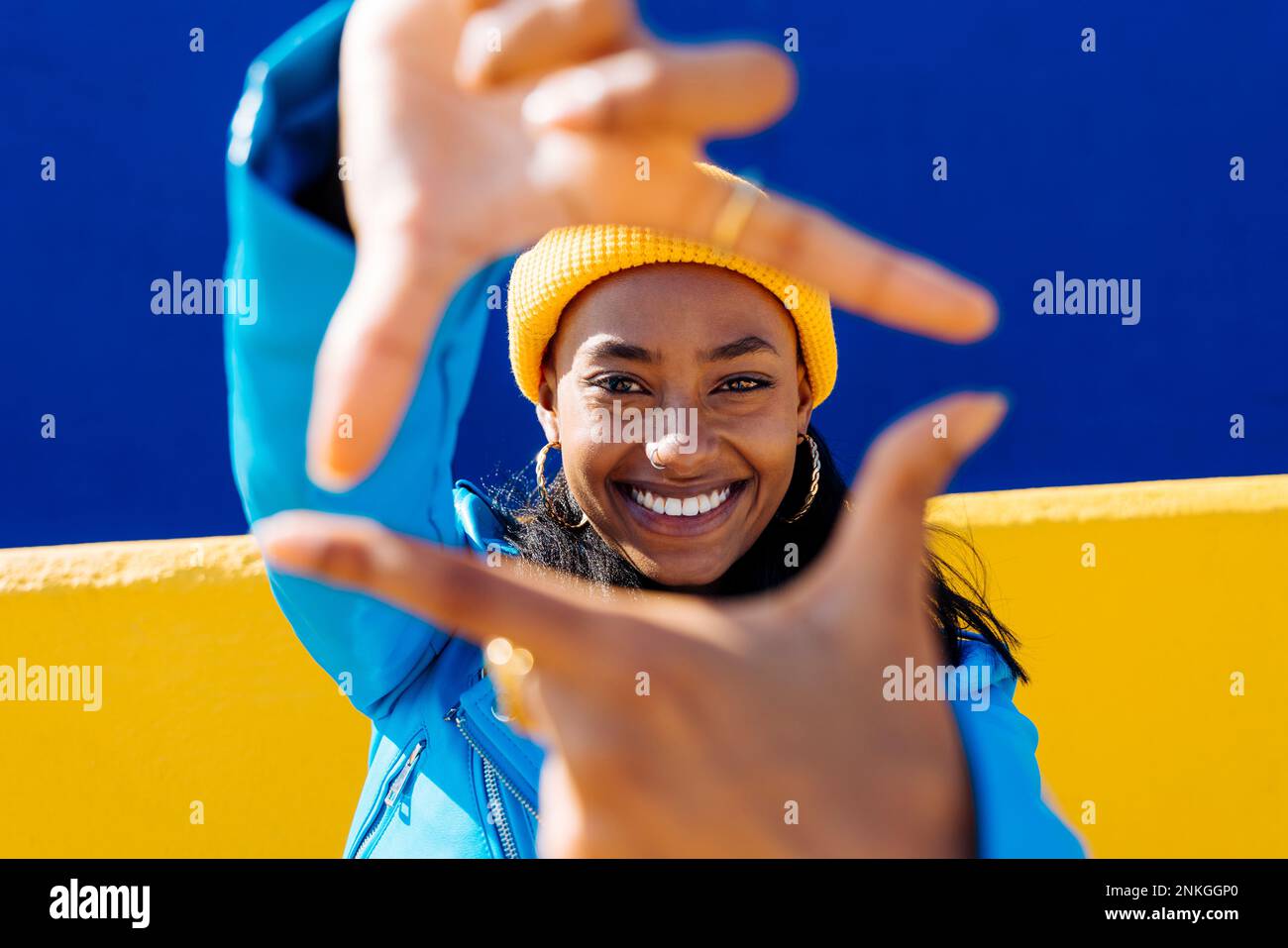 Happy woman making finger frame in front of two-tone color wall Stock ...