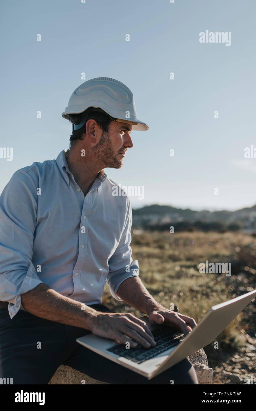 Thoughtful mature architect sitting with laptop in construction area ...