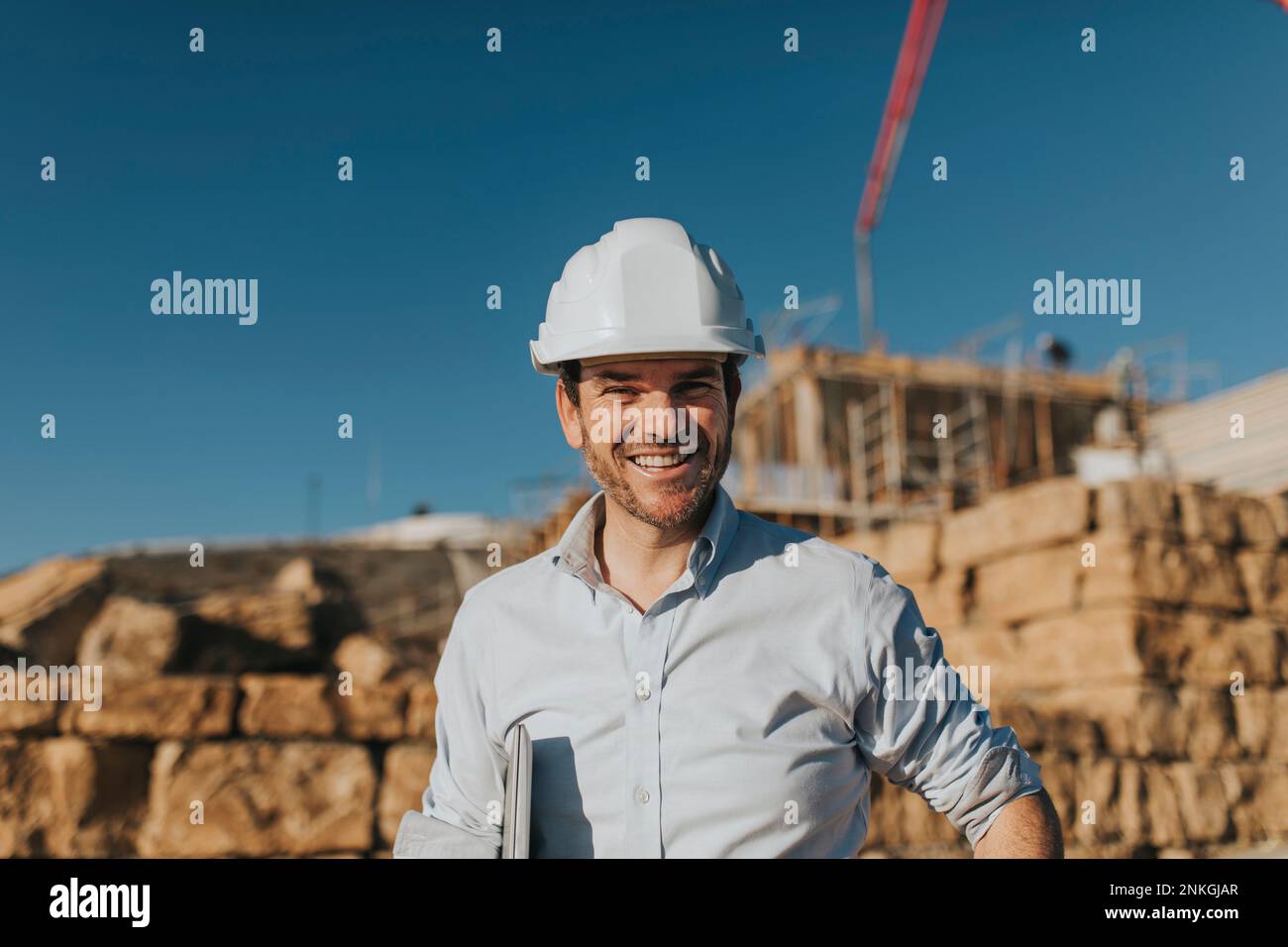 Happy architect wearing hardhat standing at construction site Stock ...