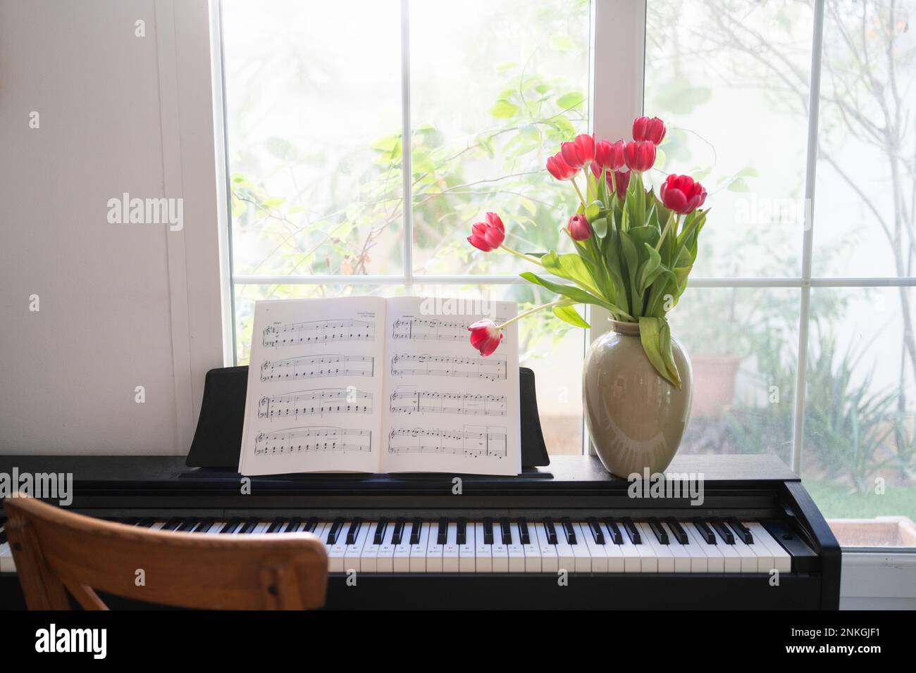 Piano with bouquet of tulips and music sheets in front of window at ...