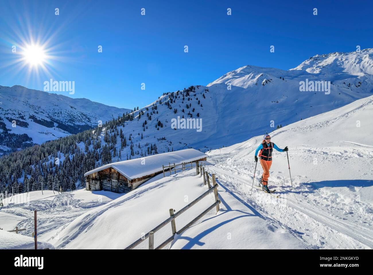Austria, Tyrol, Sun shining over female skier walking past secluded hut ...