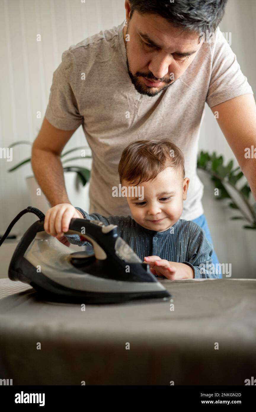 Cute son helping father to iron clothes at home Stock Photo - Alamy