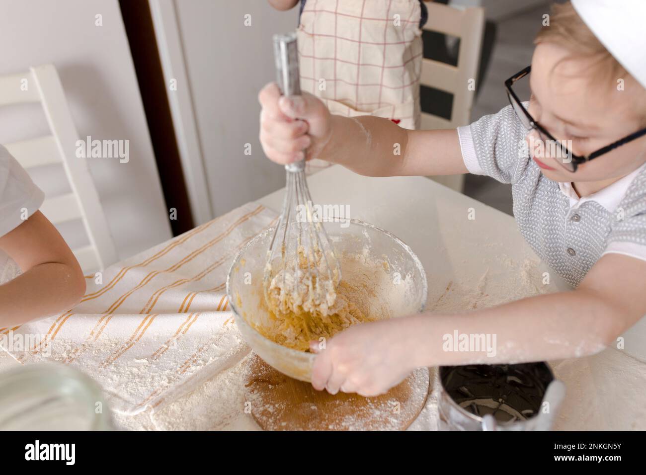 Boy with wire whisk mixing batter sitting at table Stock Photo - Alamy