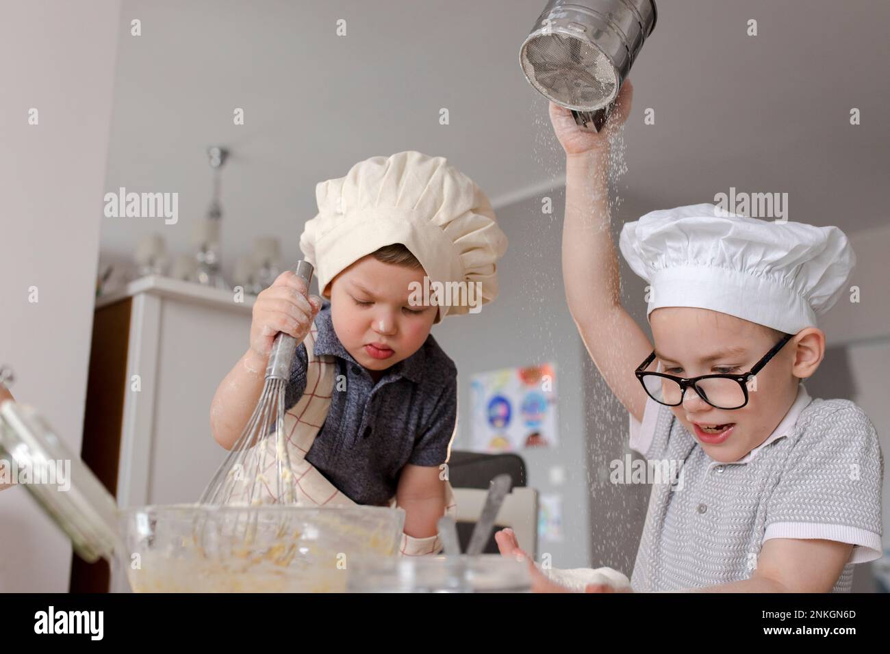 Boy sieving flour by brother mixing batter with whisk in kitchen Stock ...
