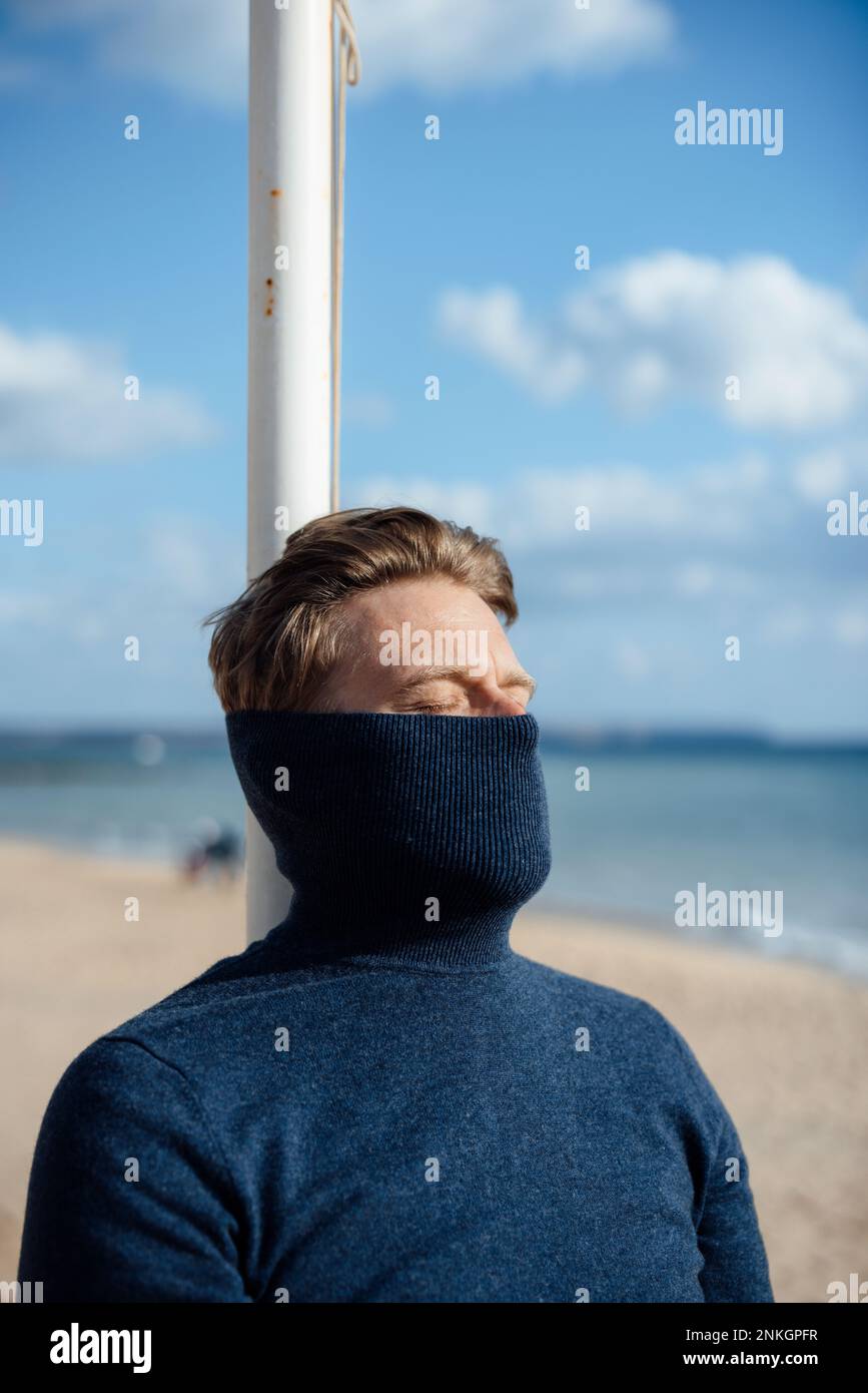Man covering face with turtleneck and relaxing at beach Stock Photo - Alamy