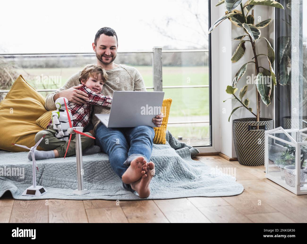 Father and son looking at laptop sitting on sofa with wind turbines ...