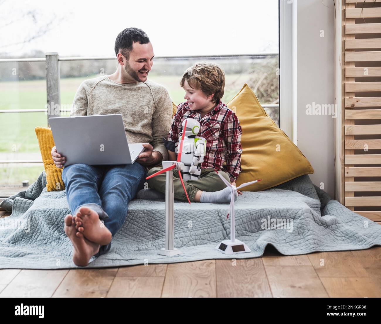 Excited father and son sitting with laptop on couch with wind turbines ...